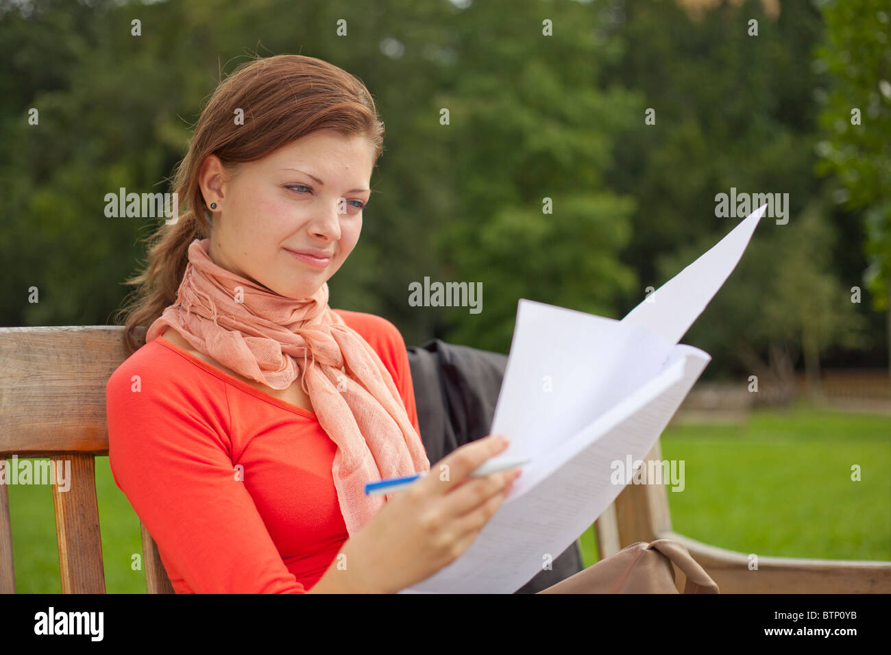Woman reading papers while sitting on a park bench, focused and ...