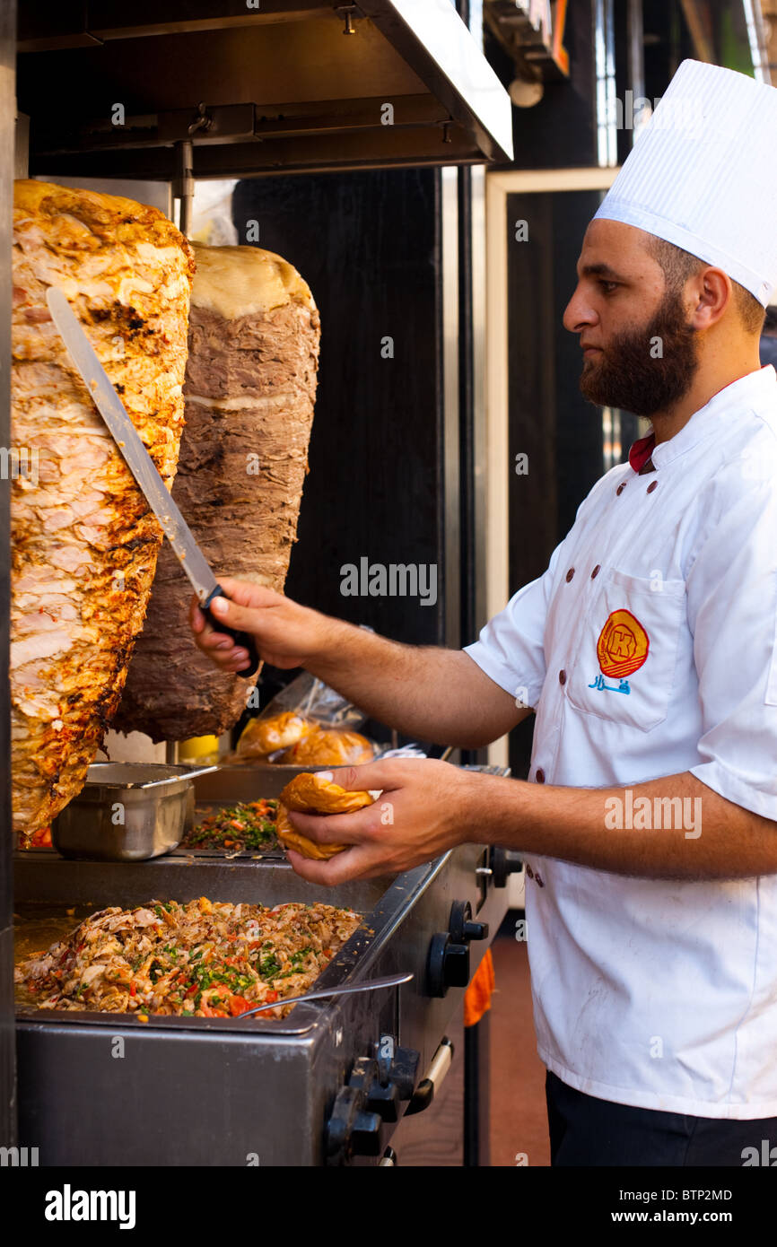 An Egyptian cook shaves slices of skewered shawerma chicken meat from a ...