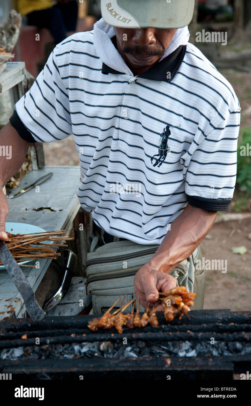 Man selling satay cooked on a charcoal burner mounted on the back of a ...