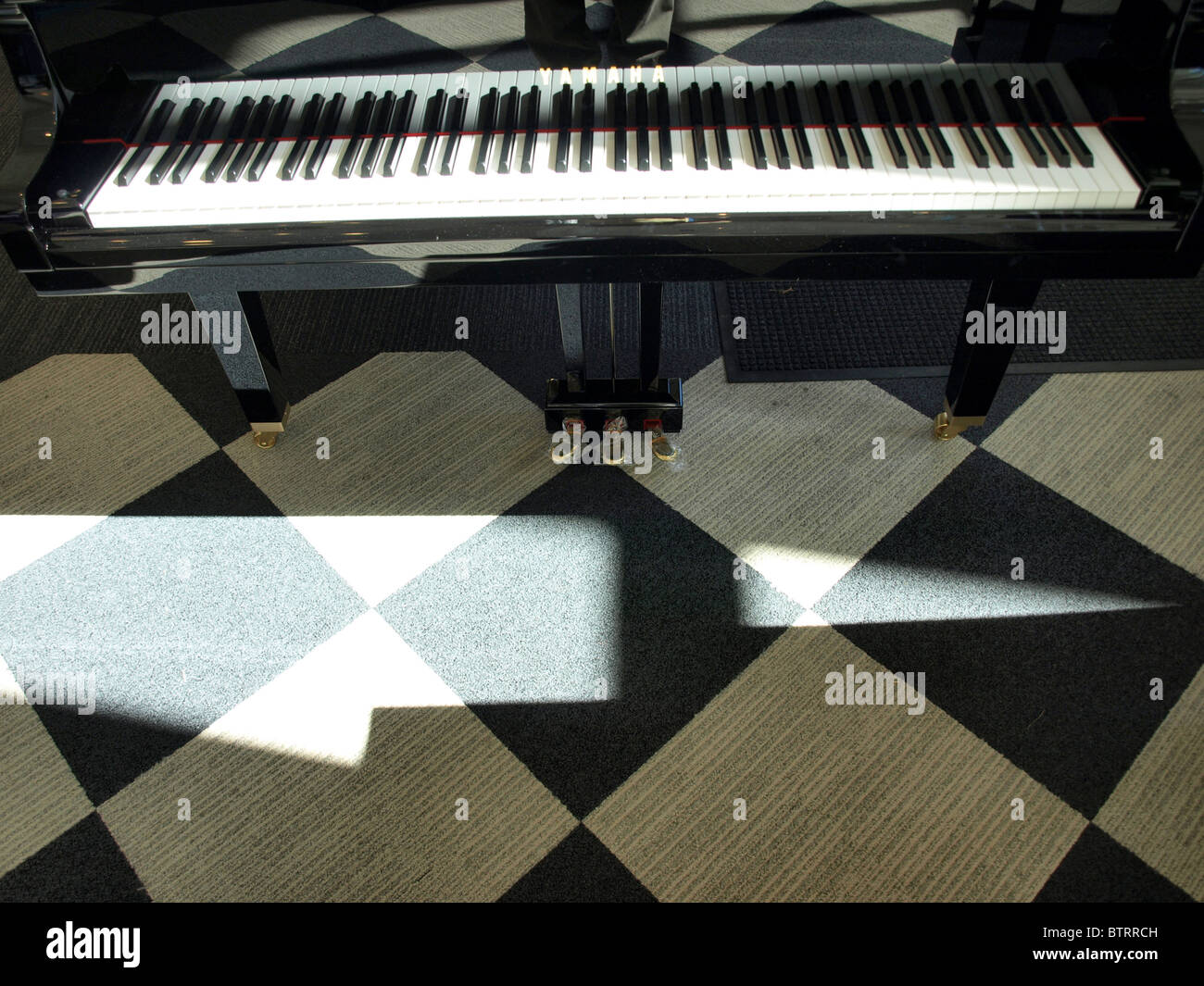 grand piano keyboard in bright sunlight on checkered carpeted floor ...