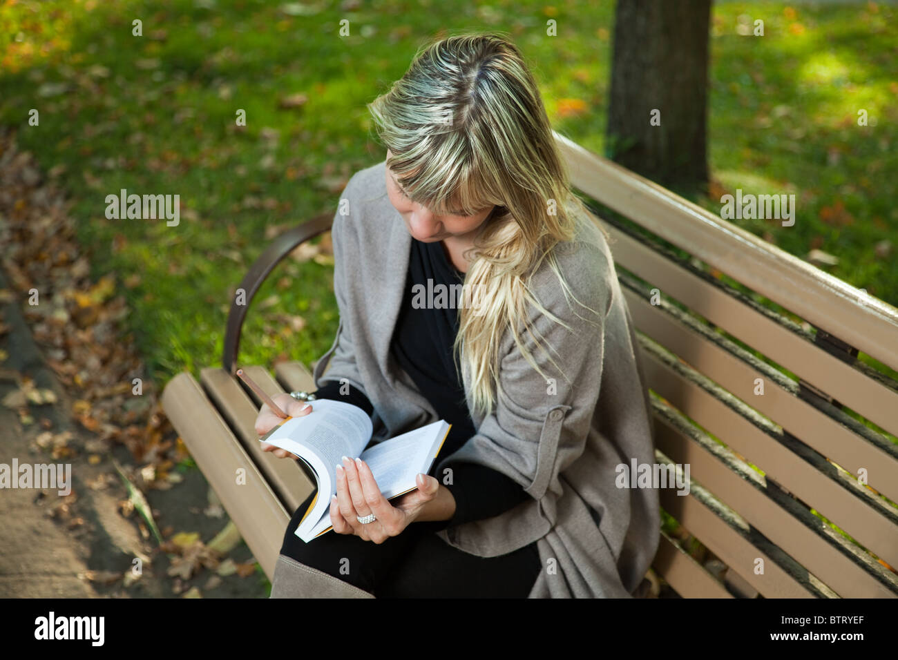 Young woman reading book with pencil in hand on a bench at an autumn ...