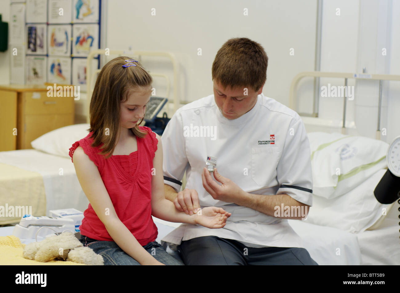 A male nurse in a hospital ward check a poorly child's pulse with his ...