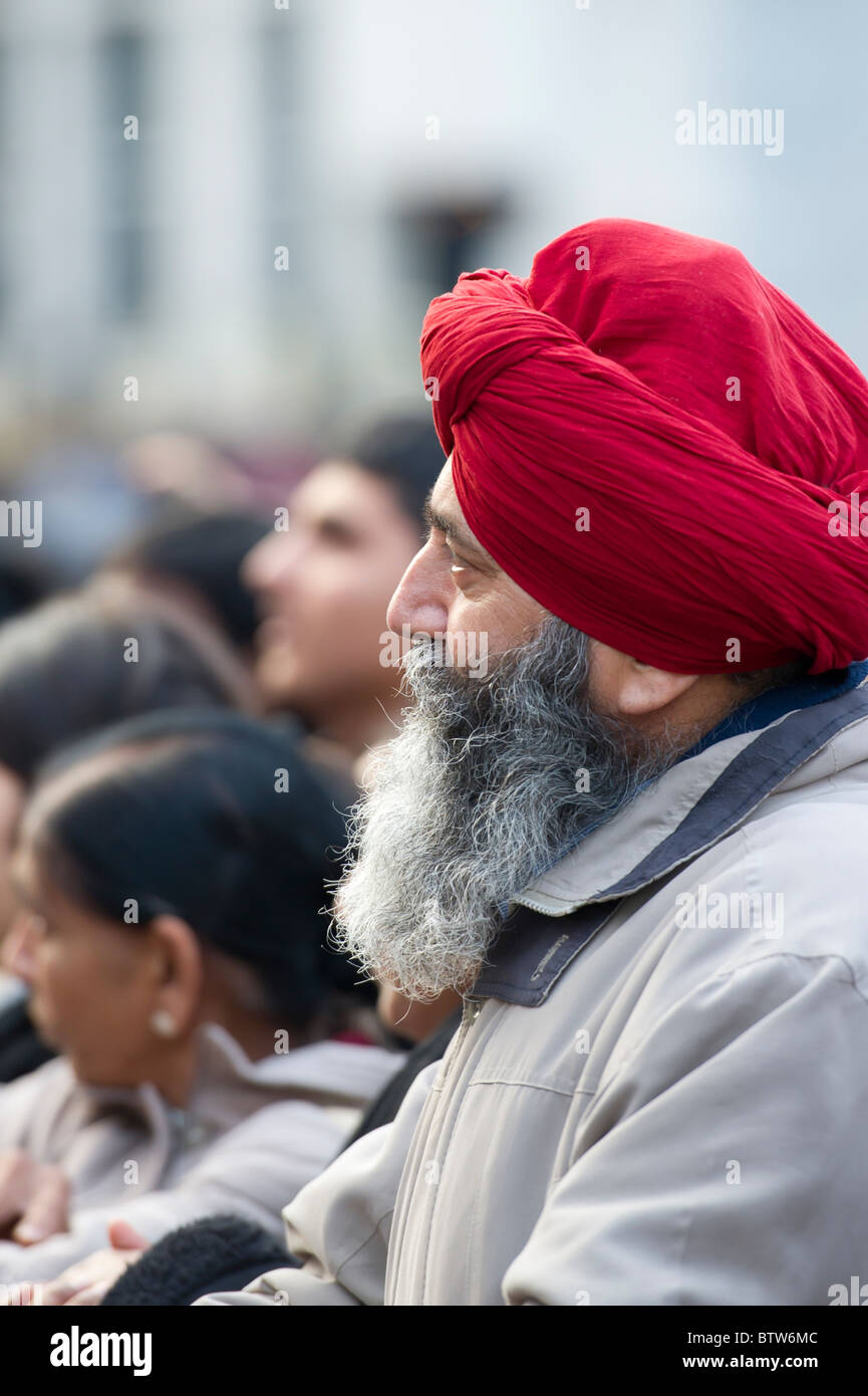A male Sikh wearing red turban, listens intently to a speech at the ...