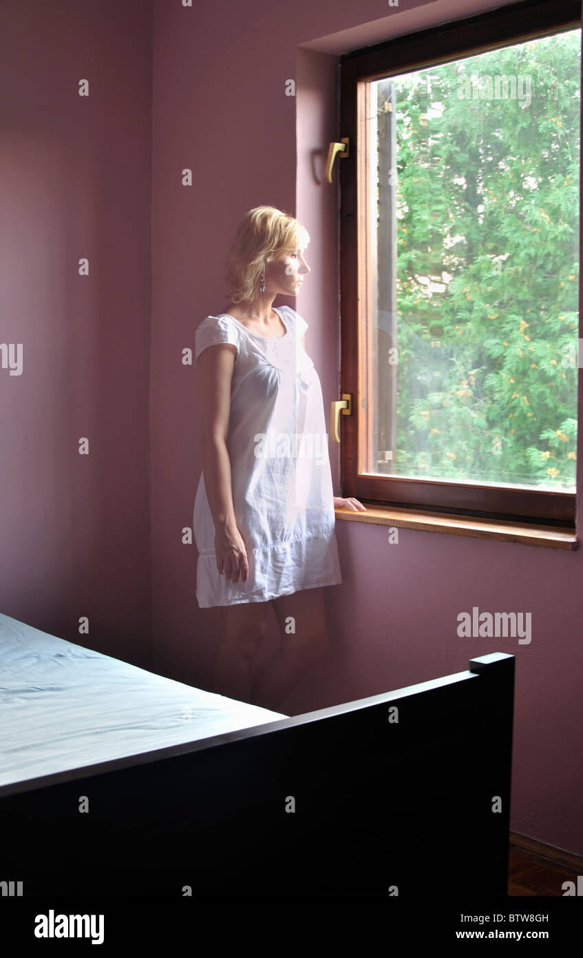 Young woman looking through window Stock Photo - Alamy
