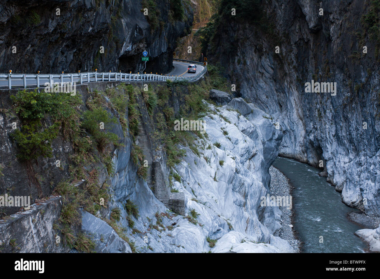 Cliffside road under rock overhang and stream flowing through marble ...