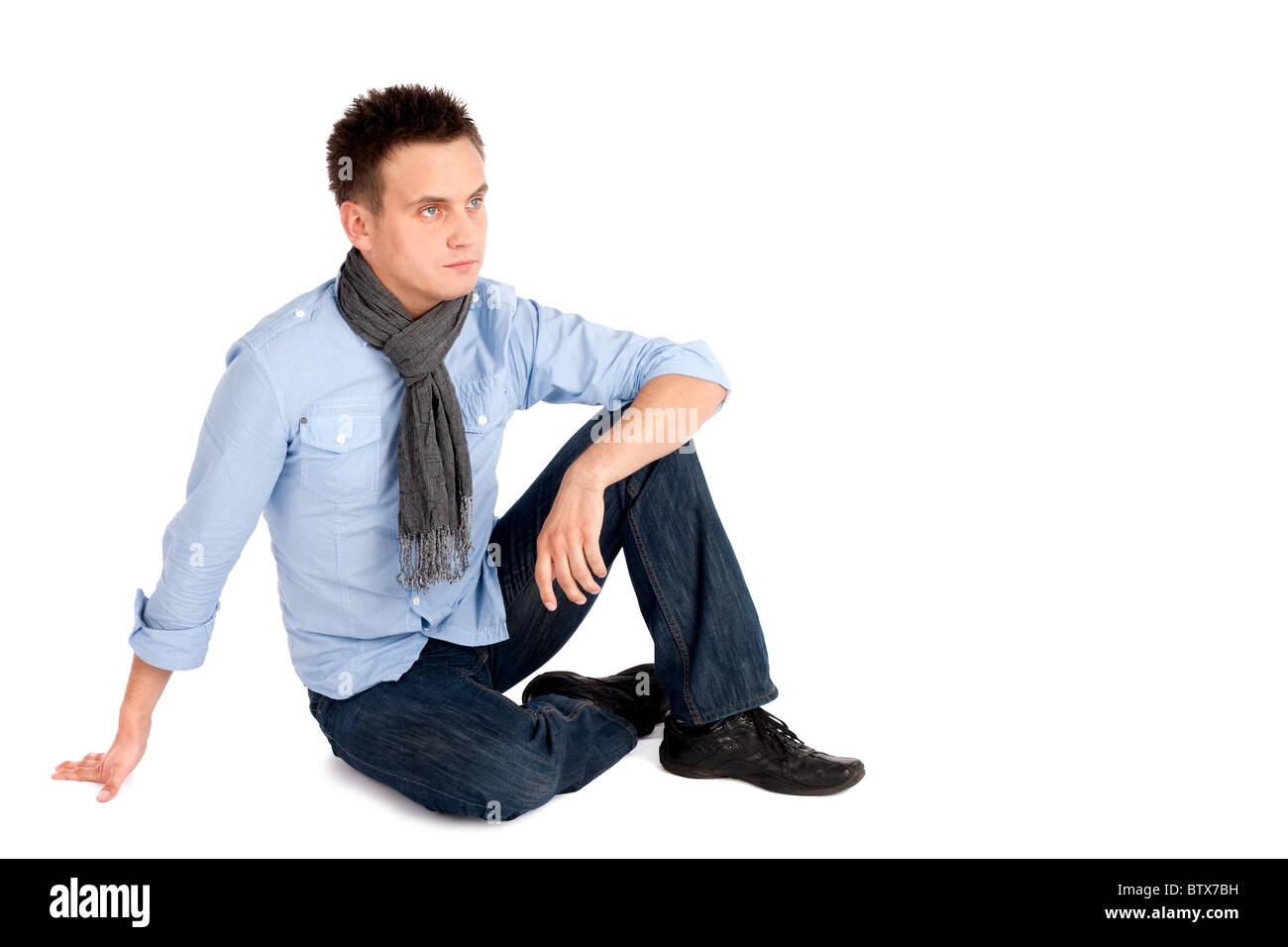 Casual young man in shirt and jeans sitting on the ground, isolated on ...