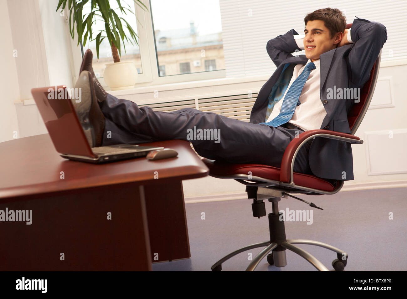 Portrait of successful businessman having rest on workplace in office ...