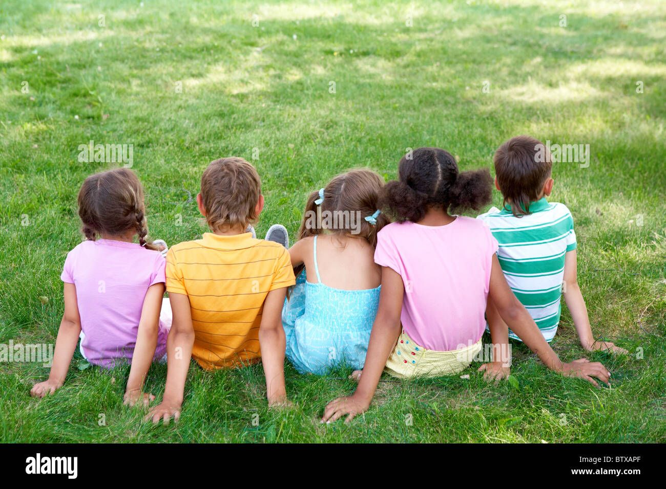 Back view of cute kids seated on green grass and relaxing Stock Photo ...