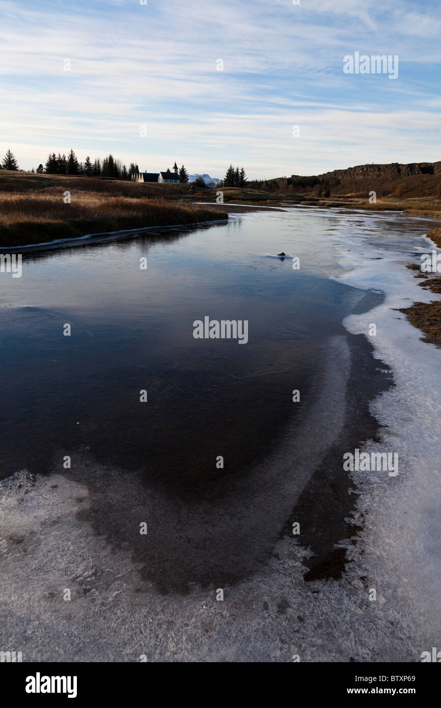Semi-frozen river Oxara with Thingvalla Kirkja church in the distance ...