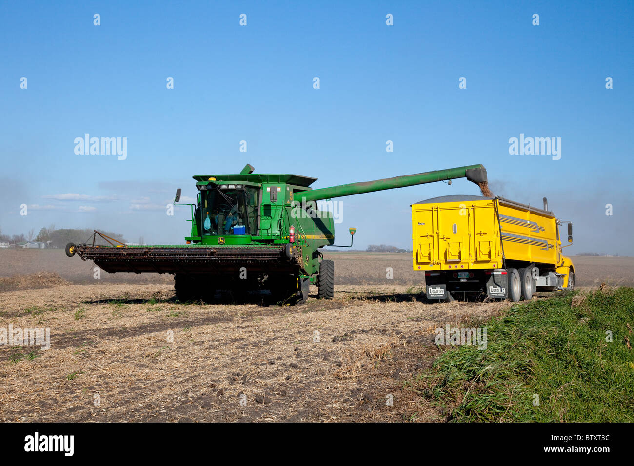A grain combine unloading beans into a truck on the Froese farm near ...