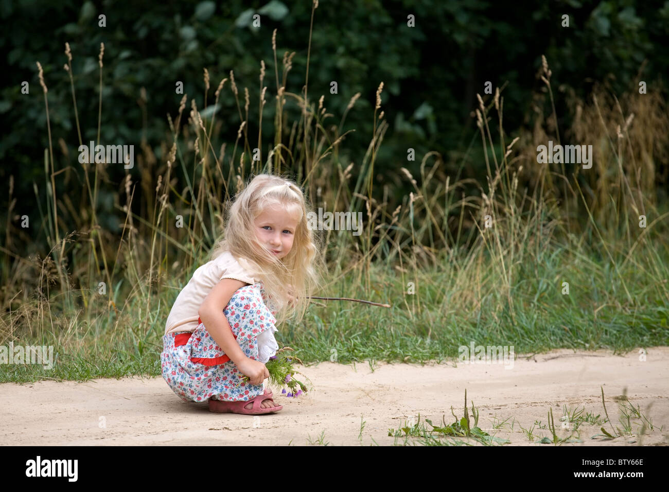 little girl sitting on park path with bunch of wild flowers Stock Photo ...