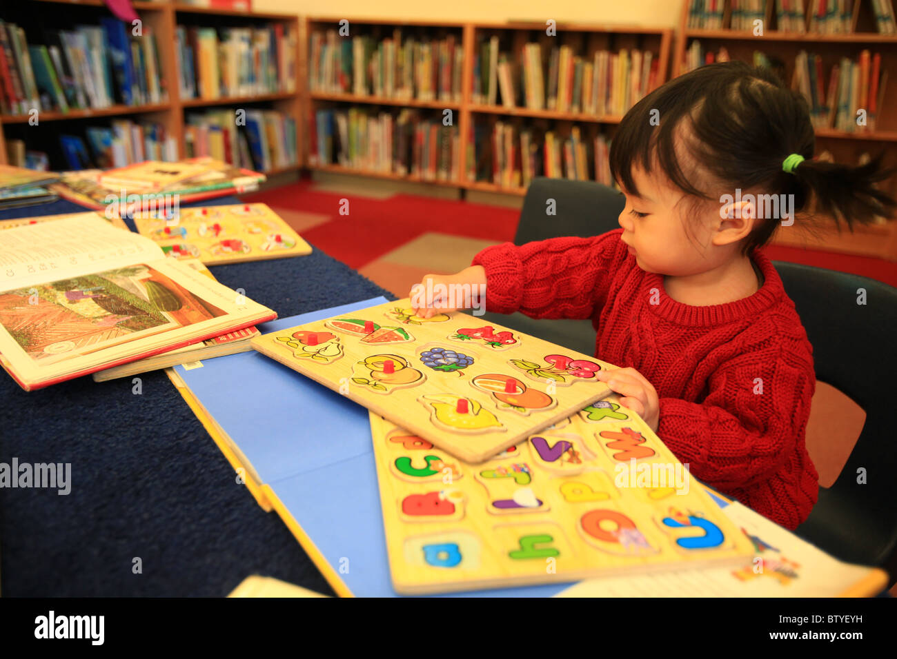 Little girl reading books in library Stock Photo - Alamy