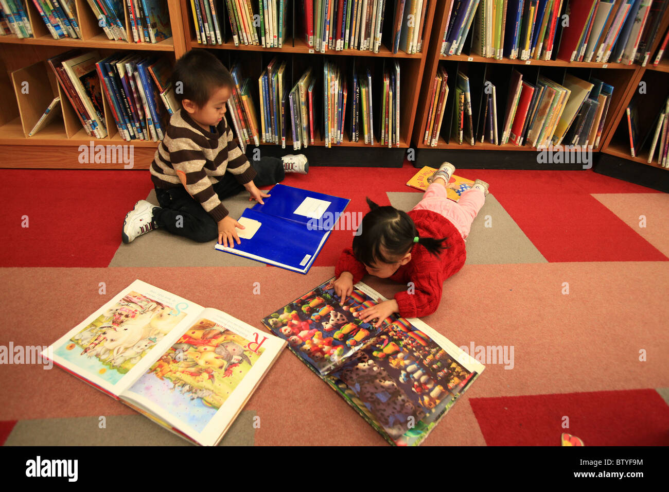 Two kids reading books in library Stock Photo - Alamy