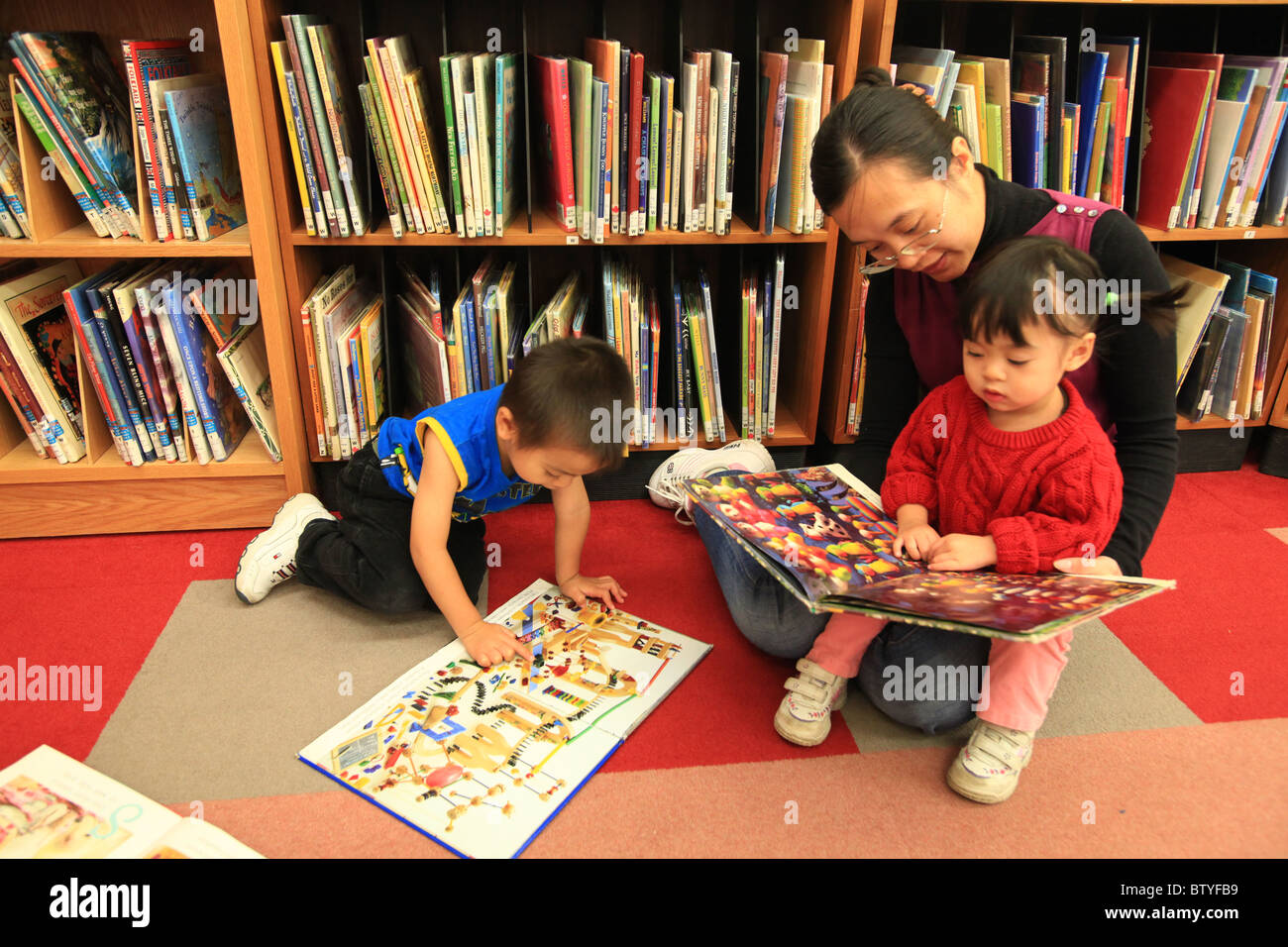 Mother reading books for her two children in library Stock Photo - Alamy