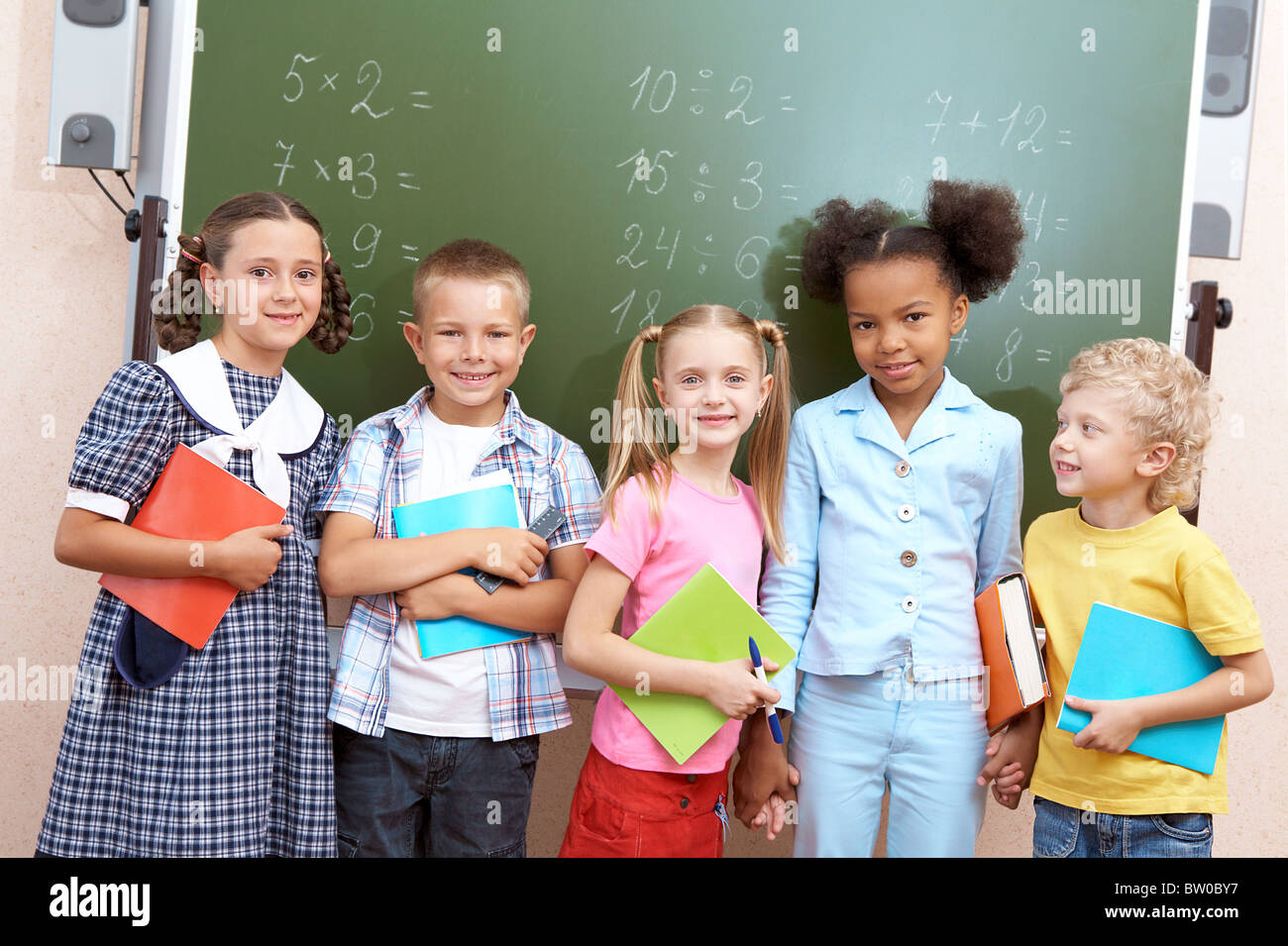 Image of curious schoolchildren standing by blackboard and looking at ...