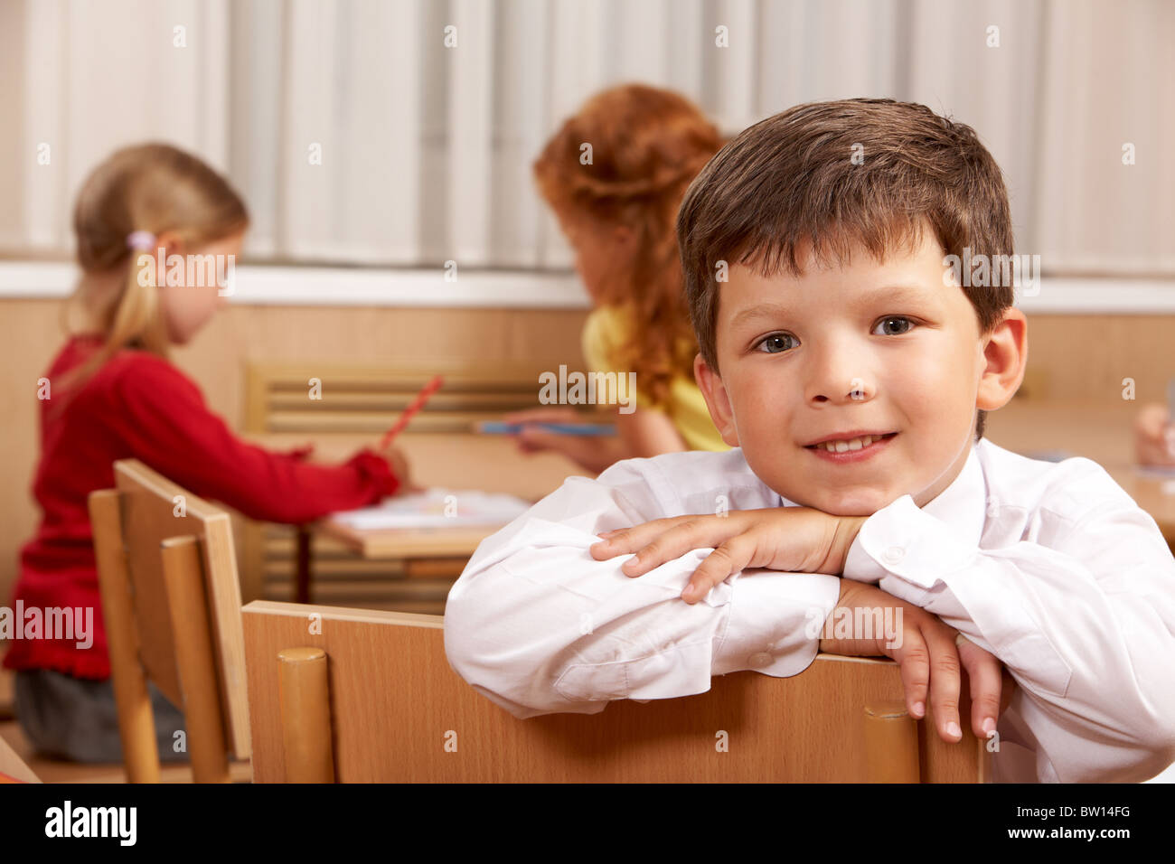Clever schoolboy looking at camera in classroom with his classmates at ...