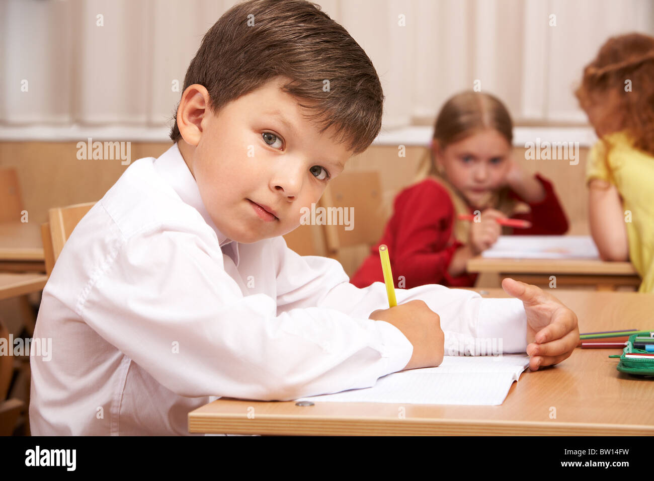 Image of smart schoolboy sitting at desk and drawing while looking at ...