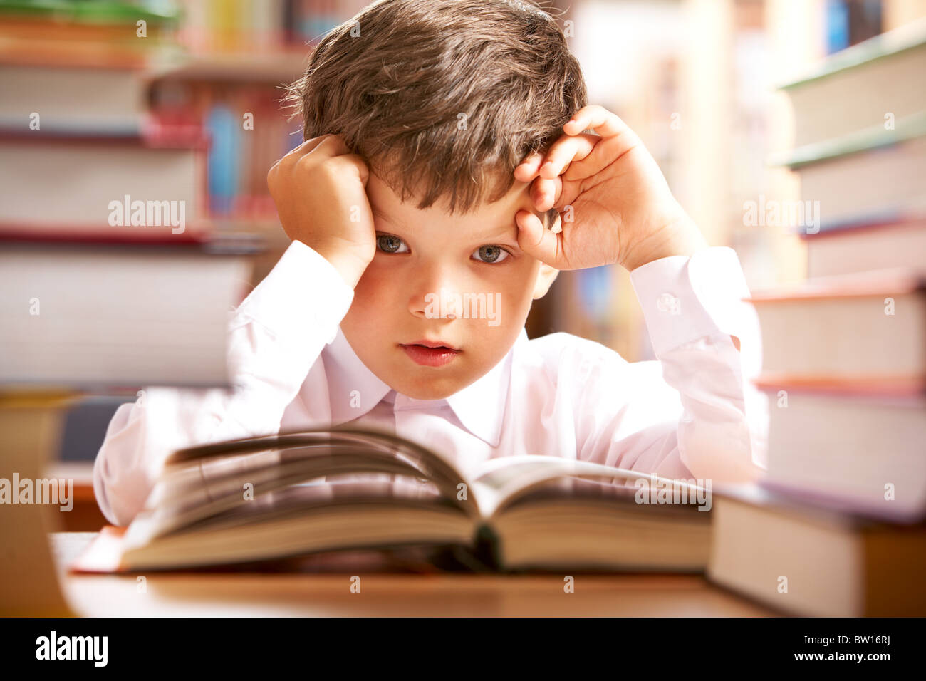 Photo of young boy looking at camera while reading book Stock Photo - Alamy