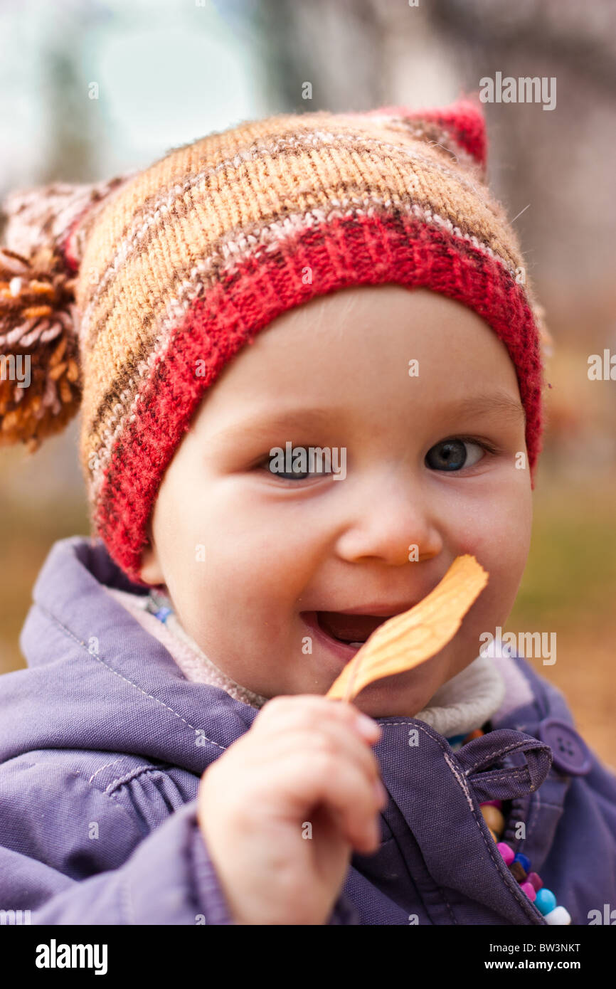 Beautiful baby with autumn leaf smiling in a funny hat outdoor against ...