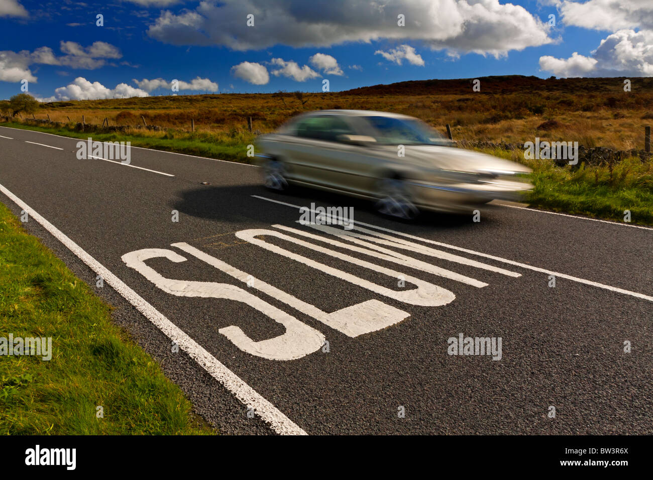 Fast moving car next to slow sign painted on country road in the UK to ...