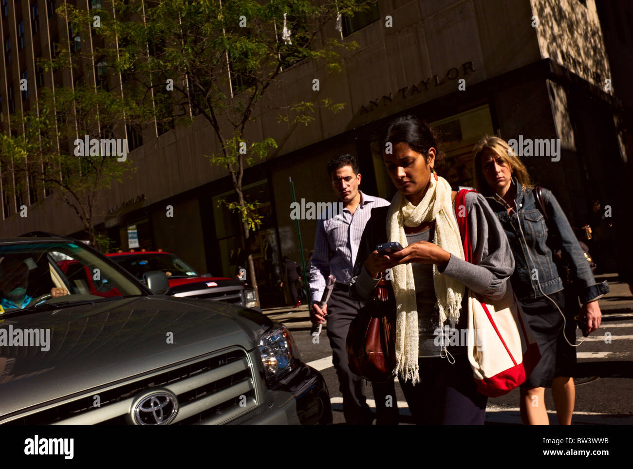 Woman texting while walking across street in front of car Stock Photo ...