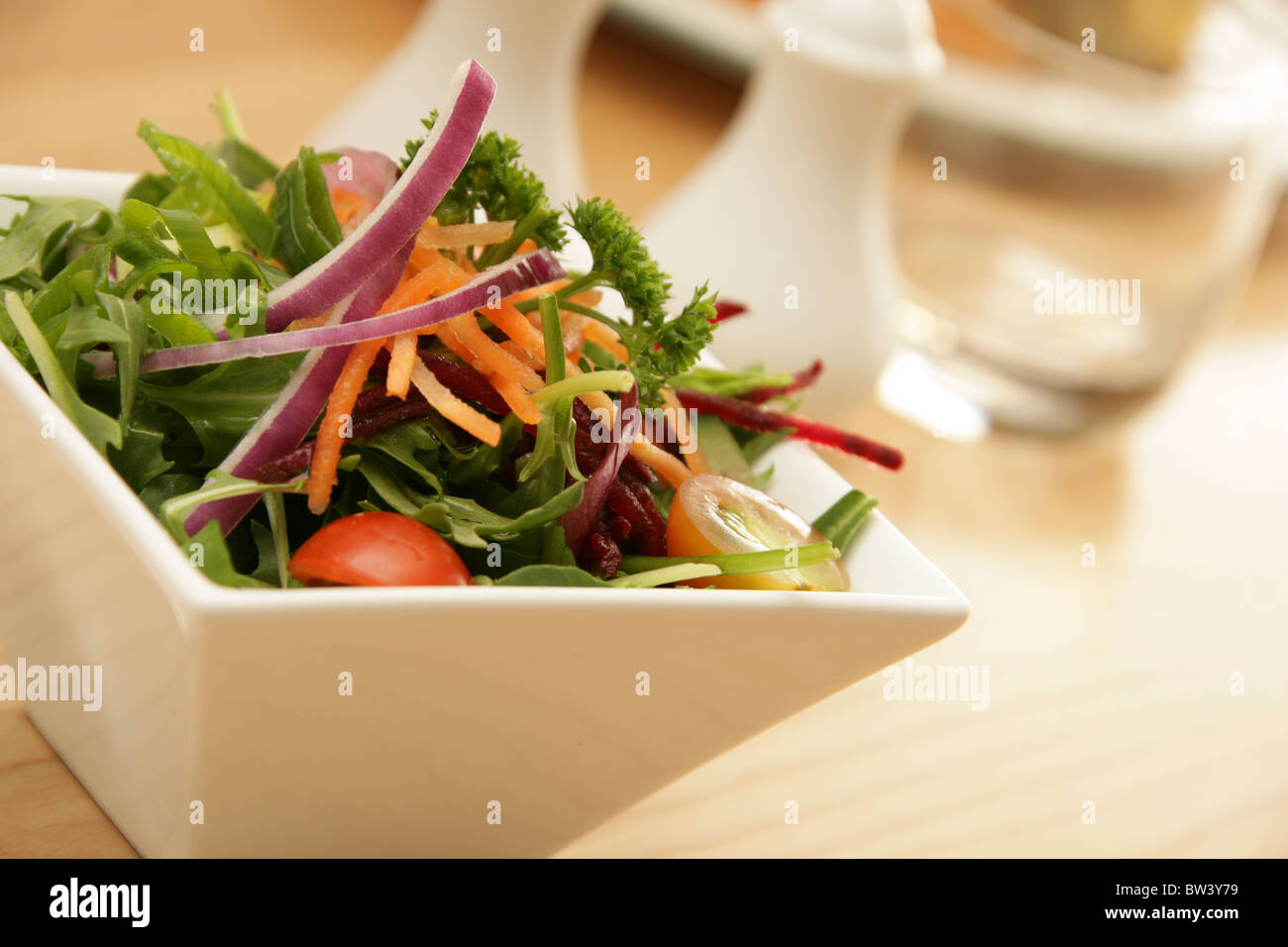 Greens salad in square bowl, dinner table setting out of focus Stock ...