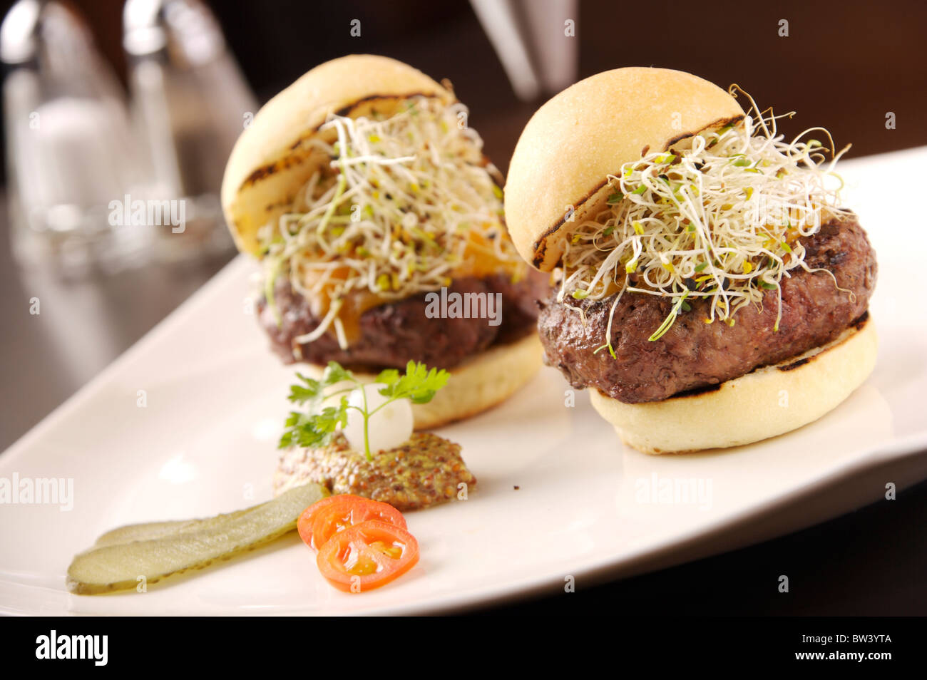 Two burgers with sprouts on white plate, dinner table setting Stock ...