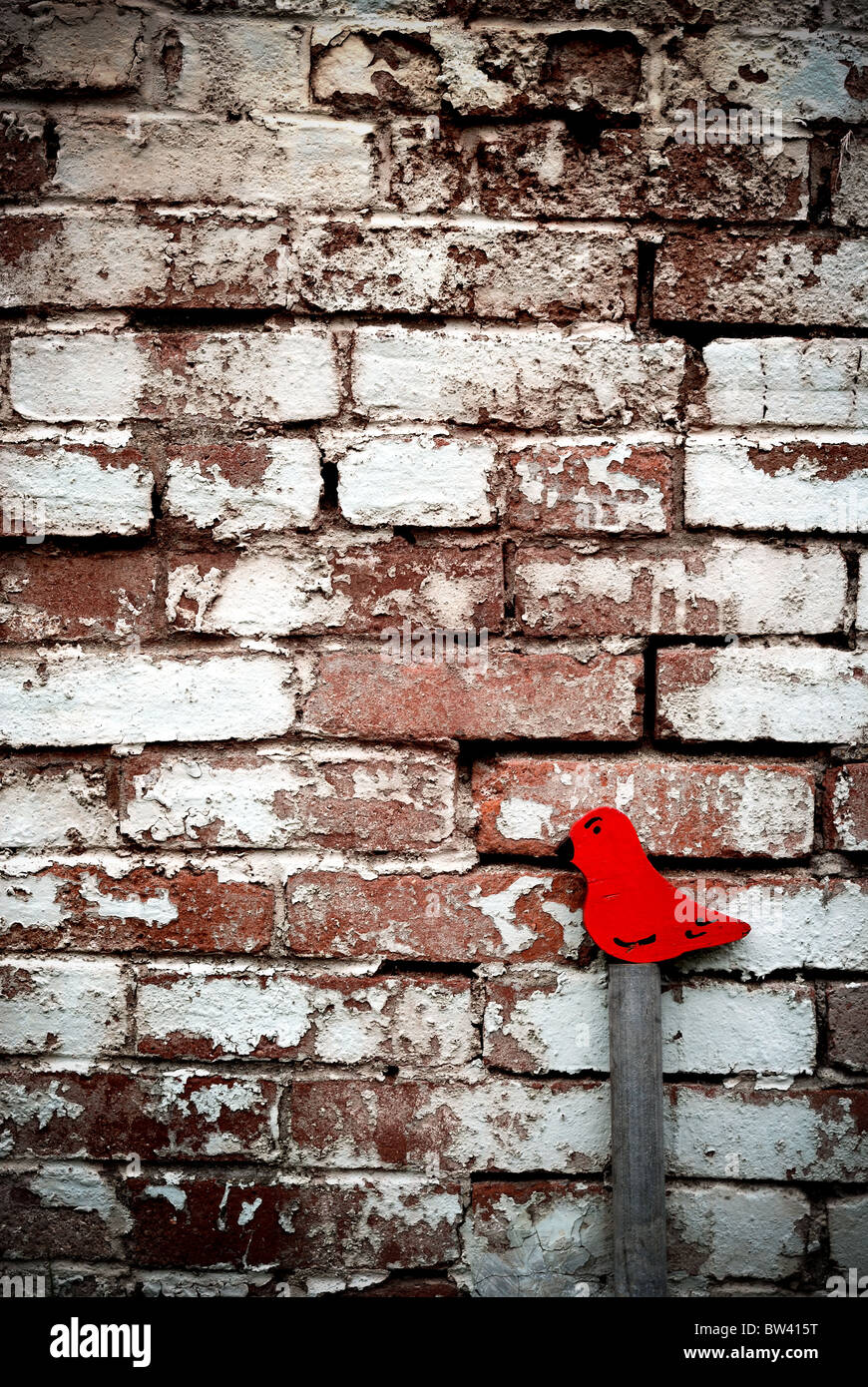 A wooden red bird, perhaps a cardinal, rests atop a pipe next to an old ...