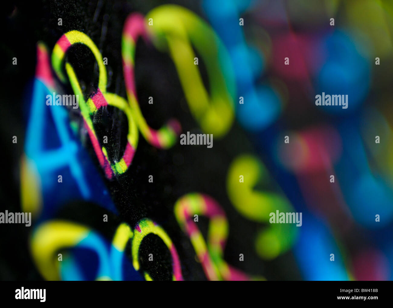 The letters of the alphabet handwritten in neon colors on black ...