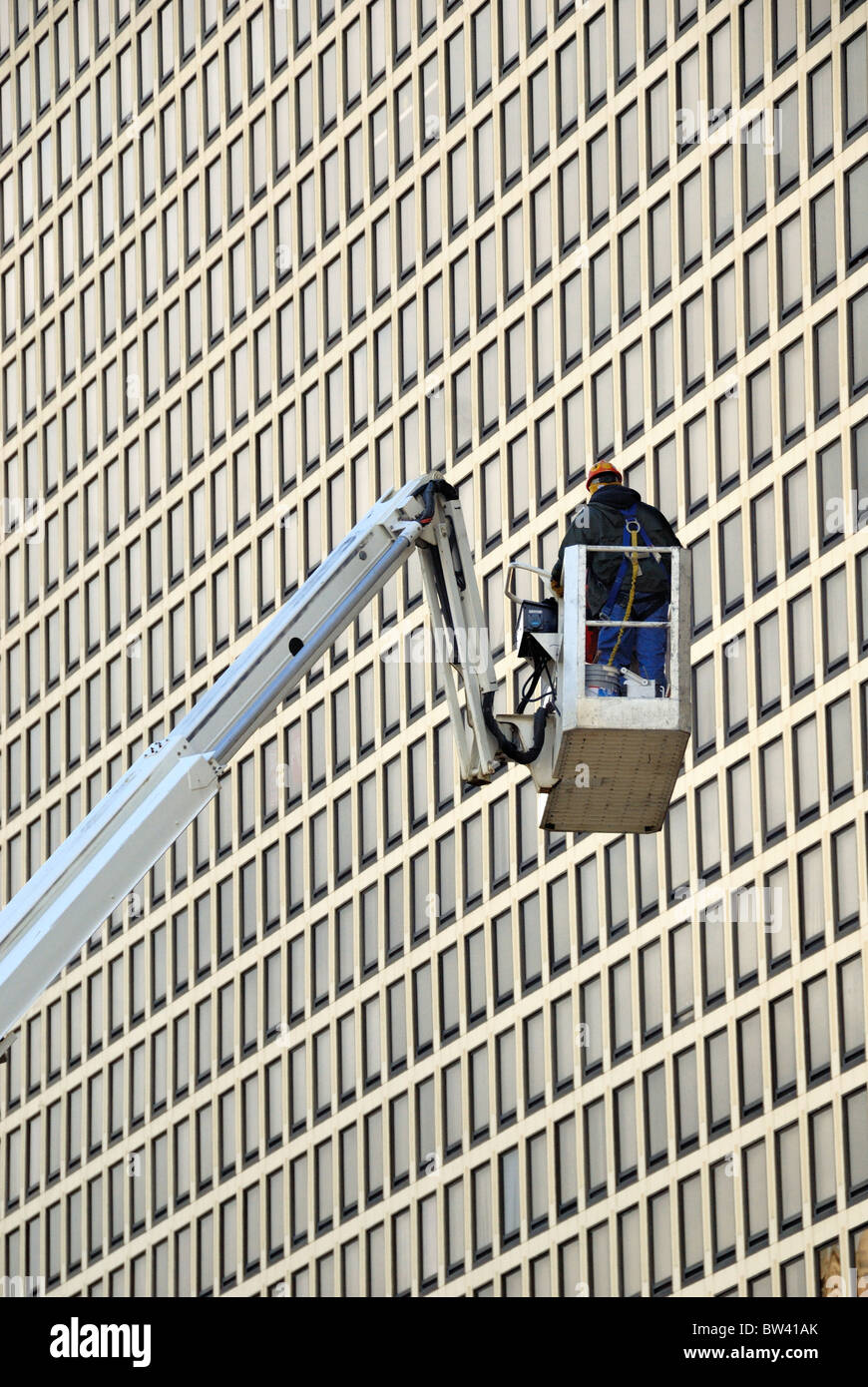 A construction worker is raised in a bucket to work on a buildingin ...
