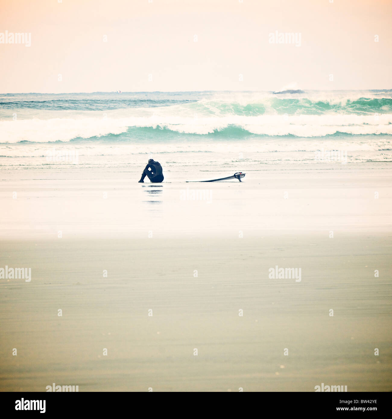 Surfer sitting on a beach in front of crashing waves, Long Beach ...