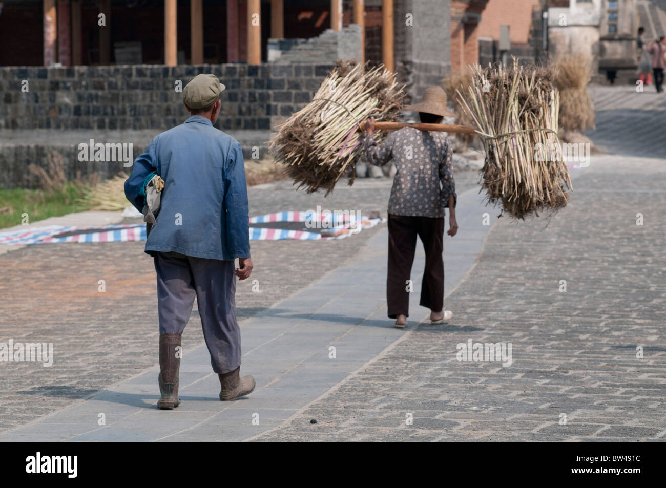 CHINA SENIOR MAN AND WOMAN CARRYING HAY IN A VILLAGE IN YUNNAN PROVINCE ...