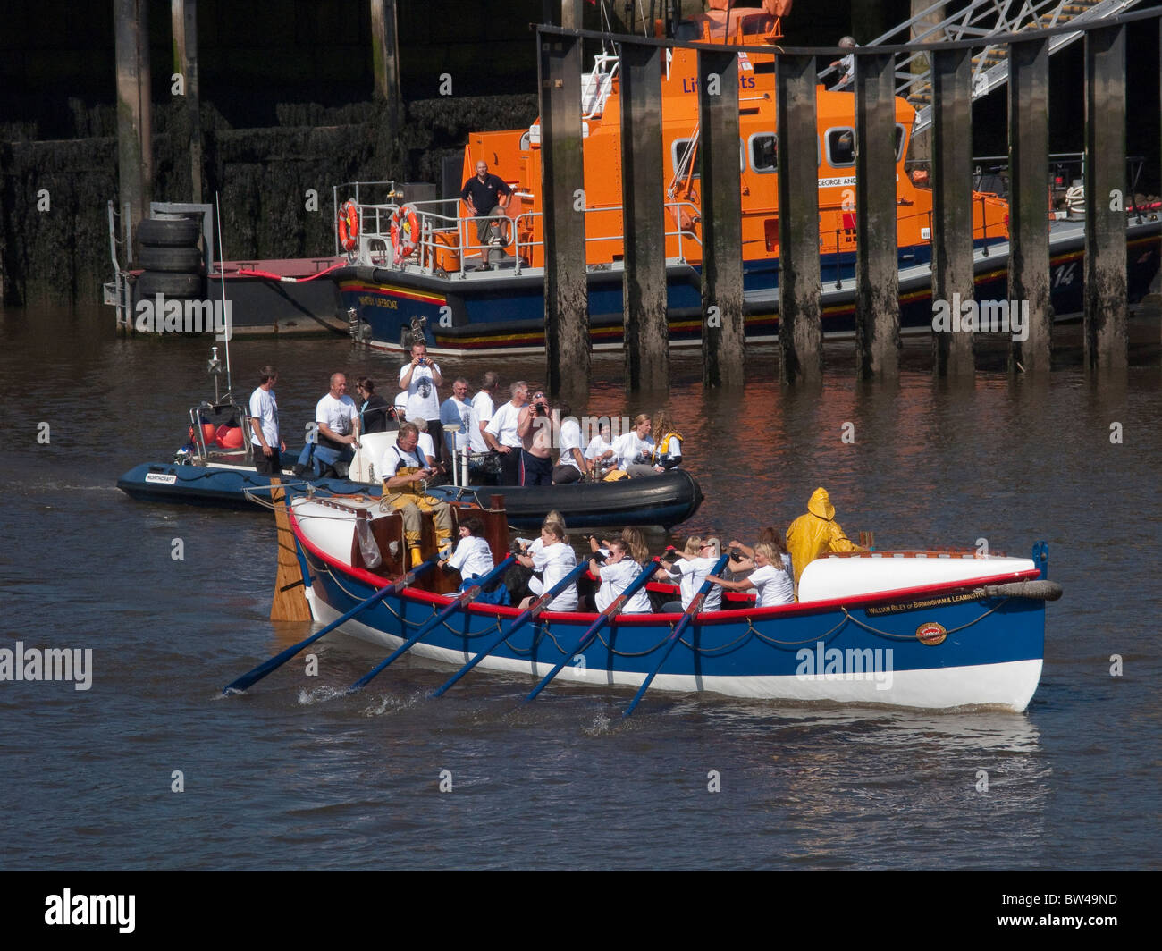 Spectators taking photos of people rowing a boat in the harbour, Whitby ...