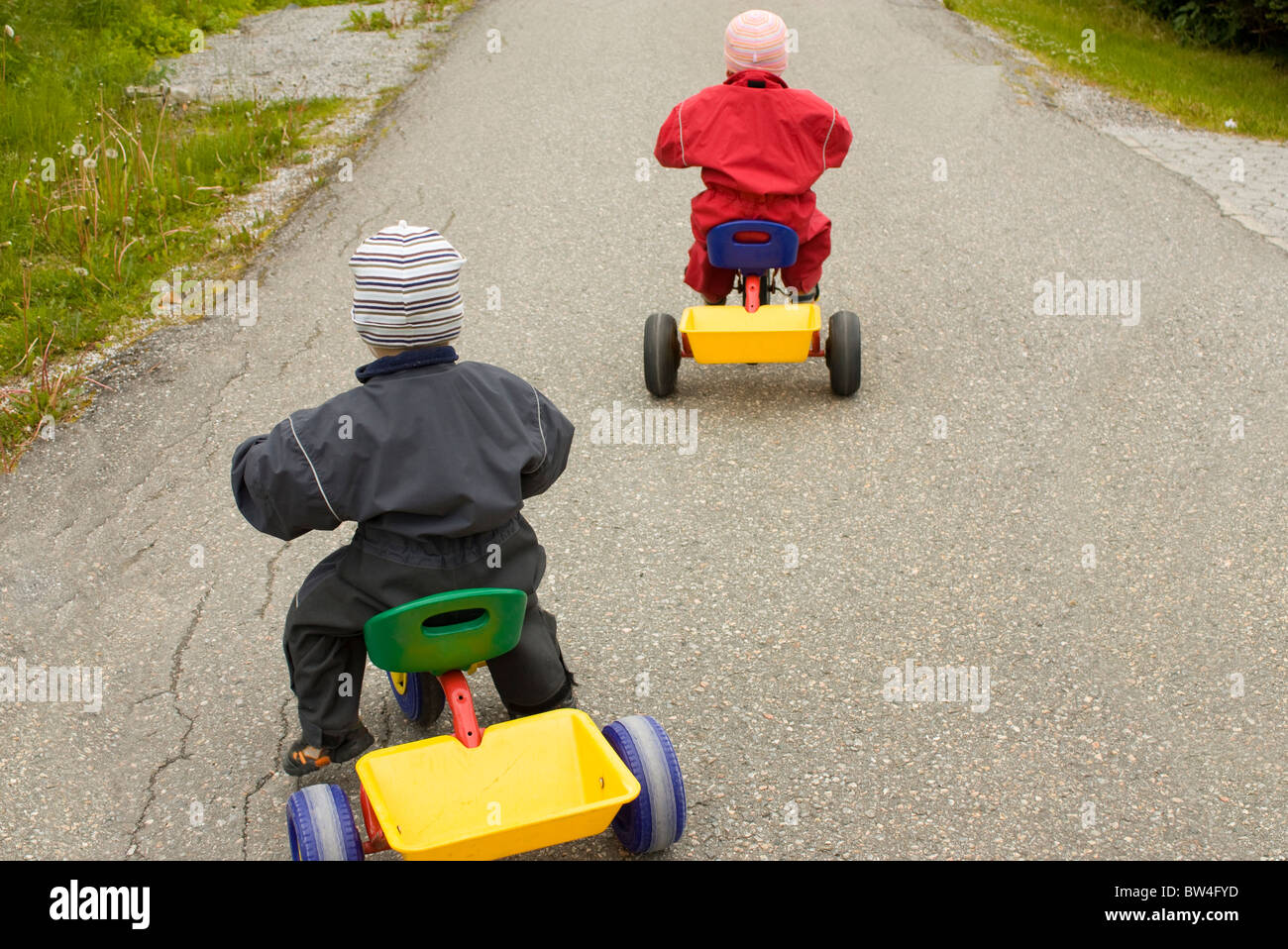 Children racing on tricycles, child in red leading in front of child in ...