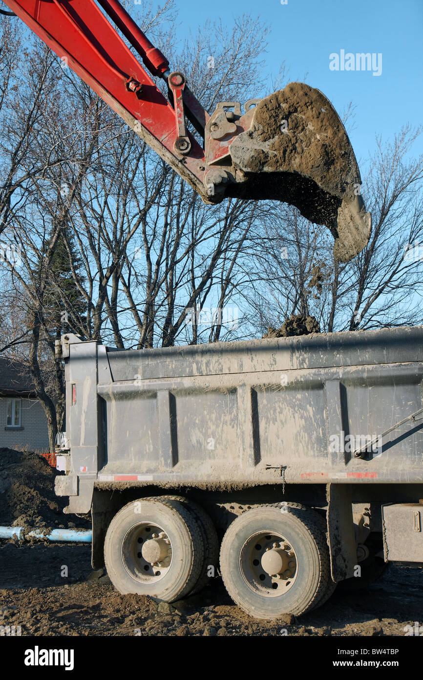 Red mechanical digger shoveling dirt into a dump truck for water line ...