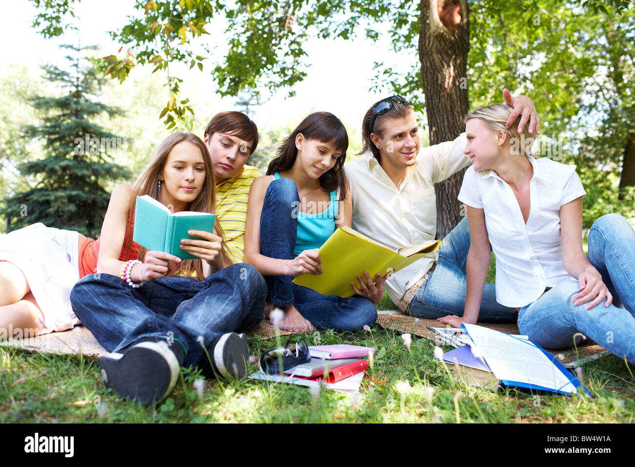 Portrait of teens talking and reading books in park at summer Stock ...