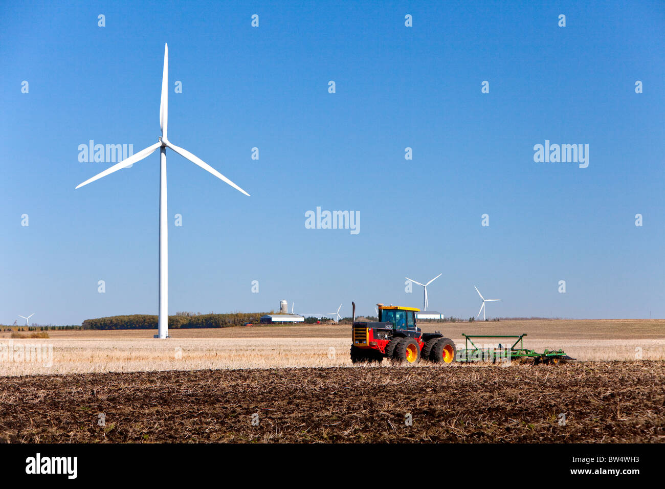A tractor working the field next to an electric wind turbine at the ...