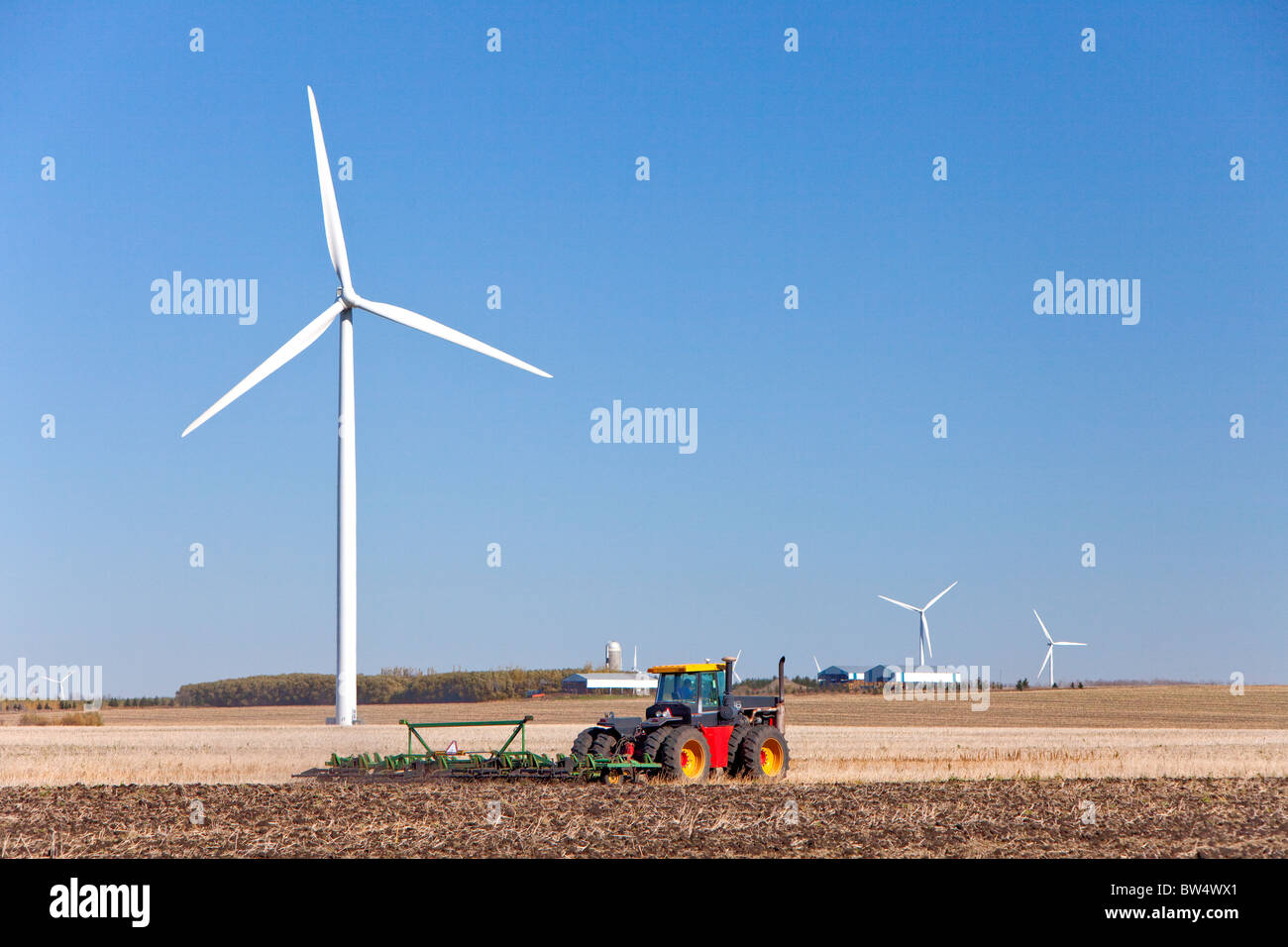 A tractor working the field next to an electric wind turbine at the ...