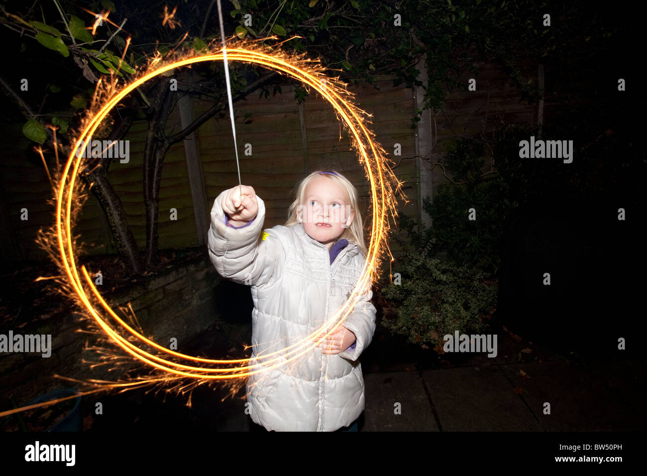 Young girl in back garden with a sparkler hand-held firework at bonfire ...