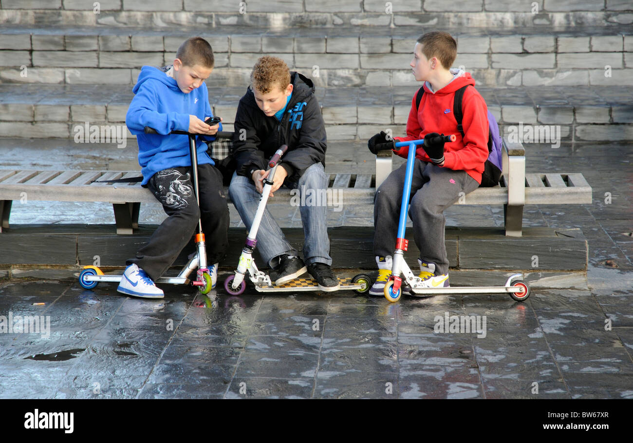 Three boys with their micro scooters sitting on a bench Stock Photo - Alamy