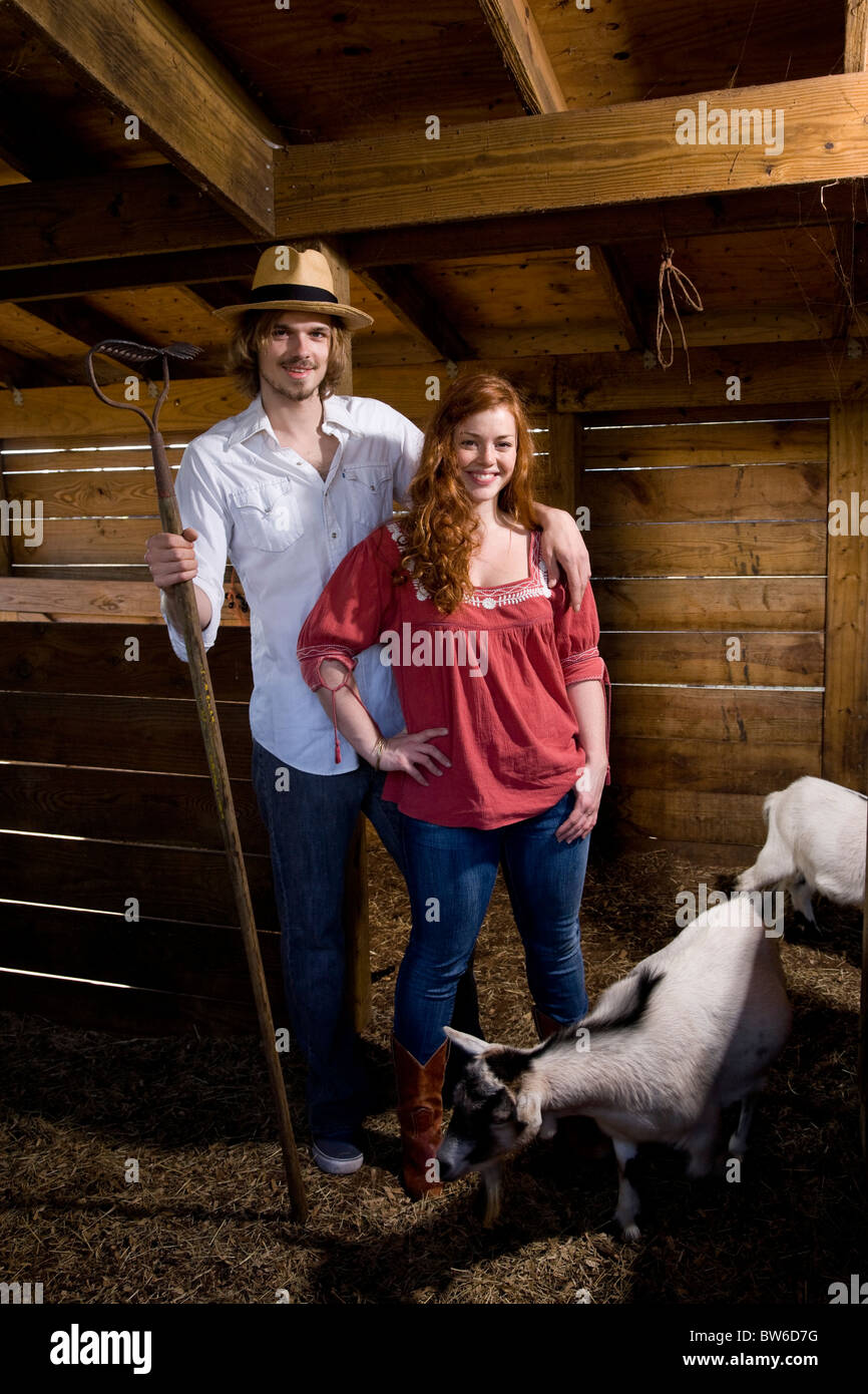 Young couple standing inside barn with goats Stock Photo - Alamy