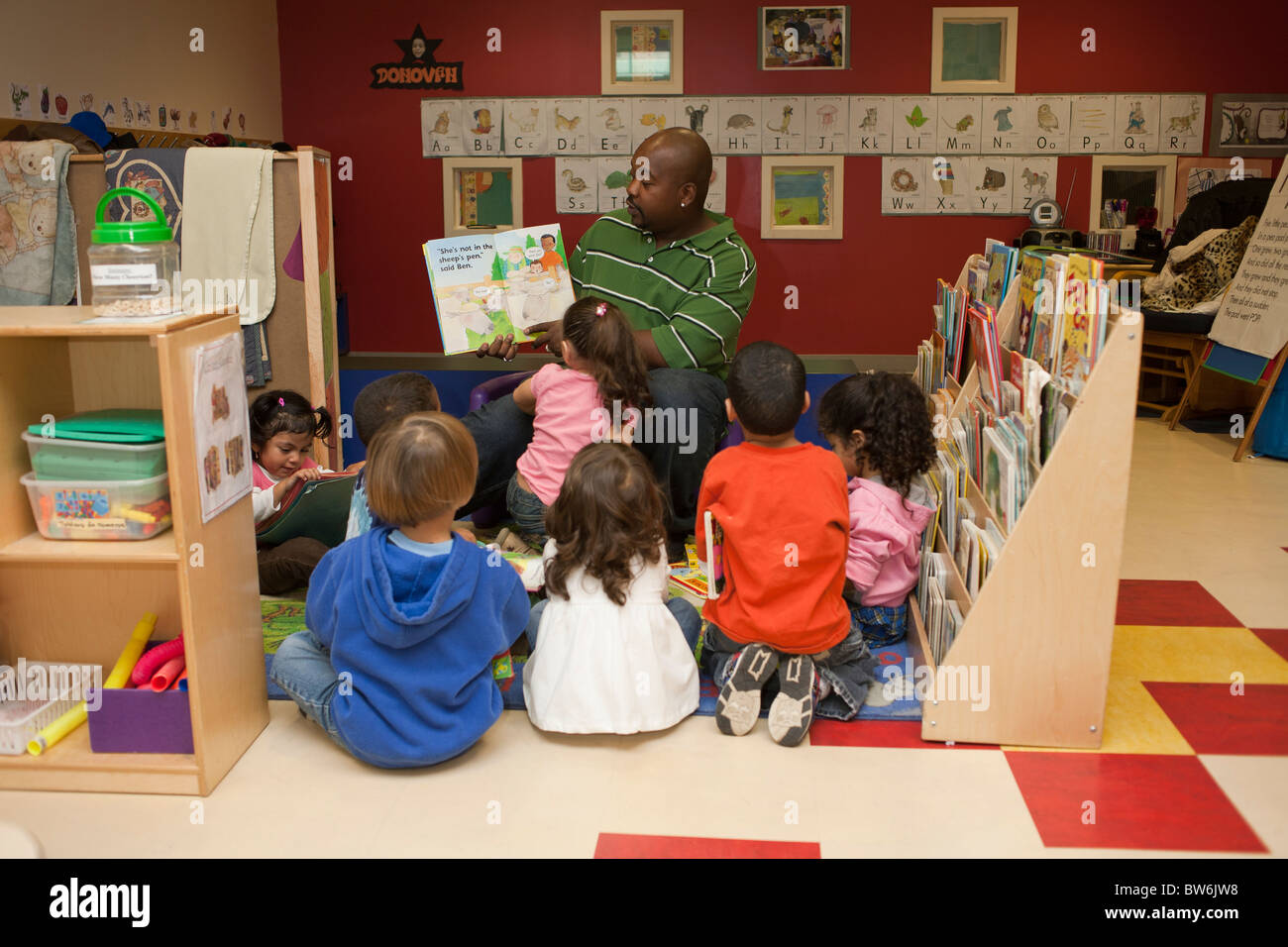 Male African-American preschool teacher helping students reading a book ...