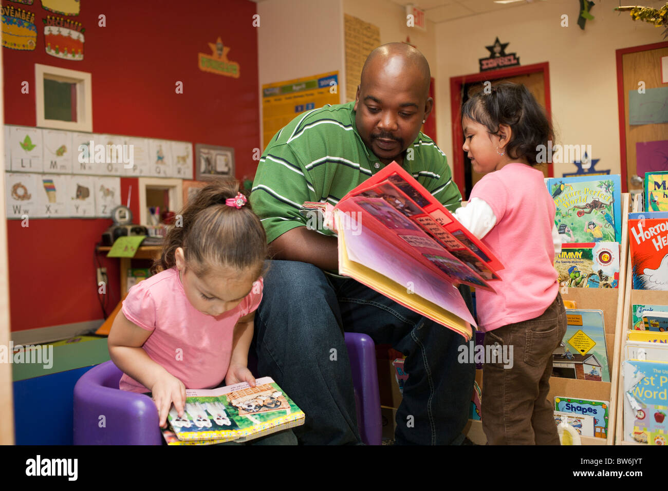 Male African-American preschool teacher helping a girl student reading ...