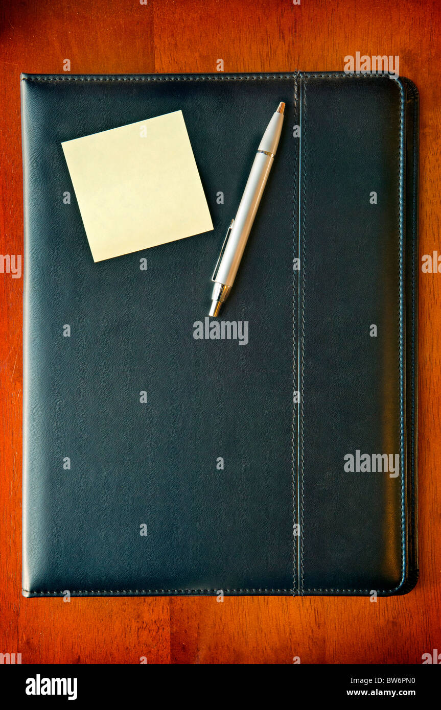 A black executive folder on timber desk with sticky note and silver pen ...