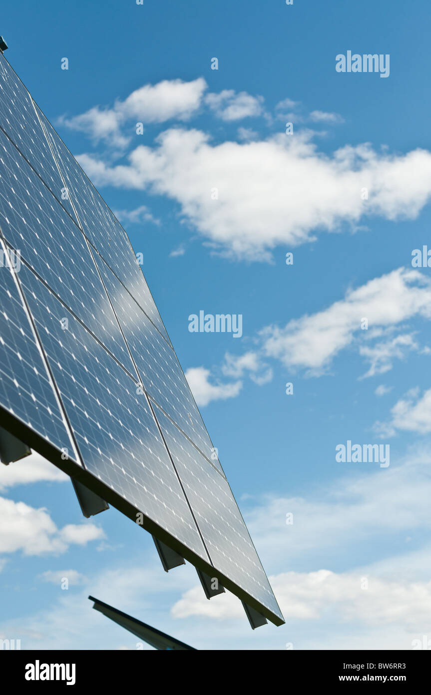 A photovoltaic solar panel array with a blue sky and puffy white clouds ...