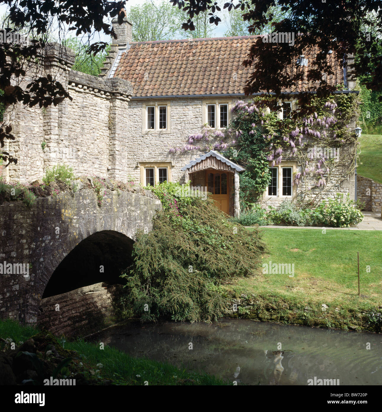 Stone bridge over stream in garden of stone-built country cottage clad ...