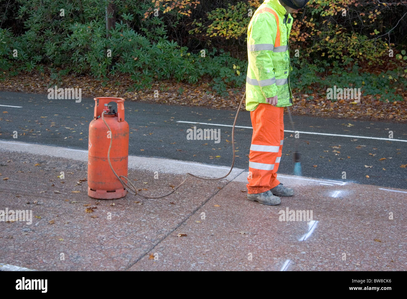 Workman preparing a road surface for line marking using a flame wand ...