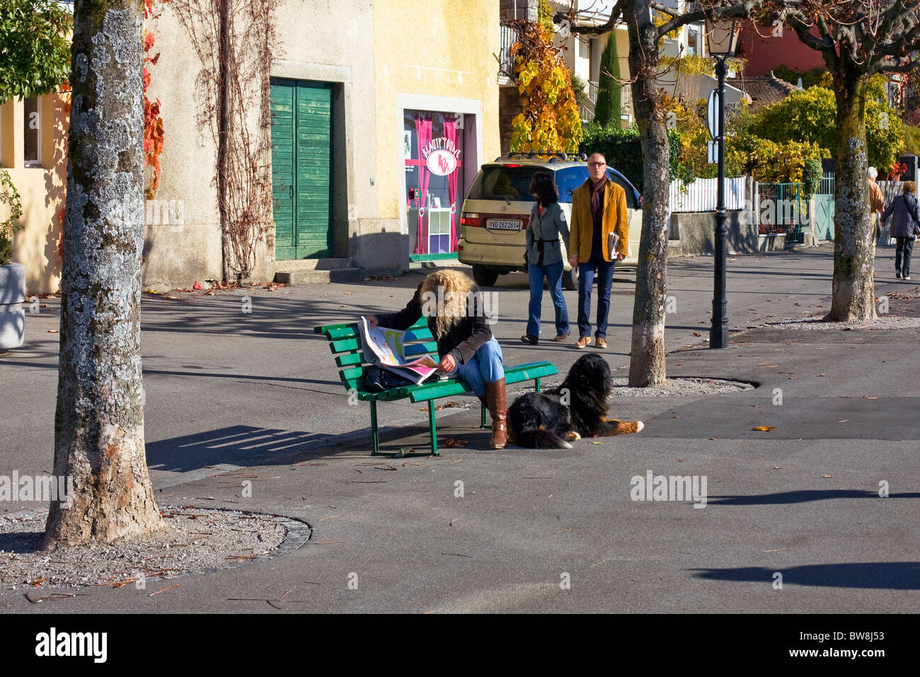 Woman reading a newspaper on a bench while others take a Sunday morning ...