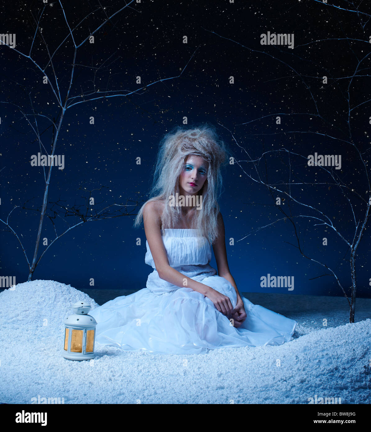 portrait of beautiful frozen fairy nymph girl sitting on snow with lamp ...