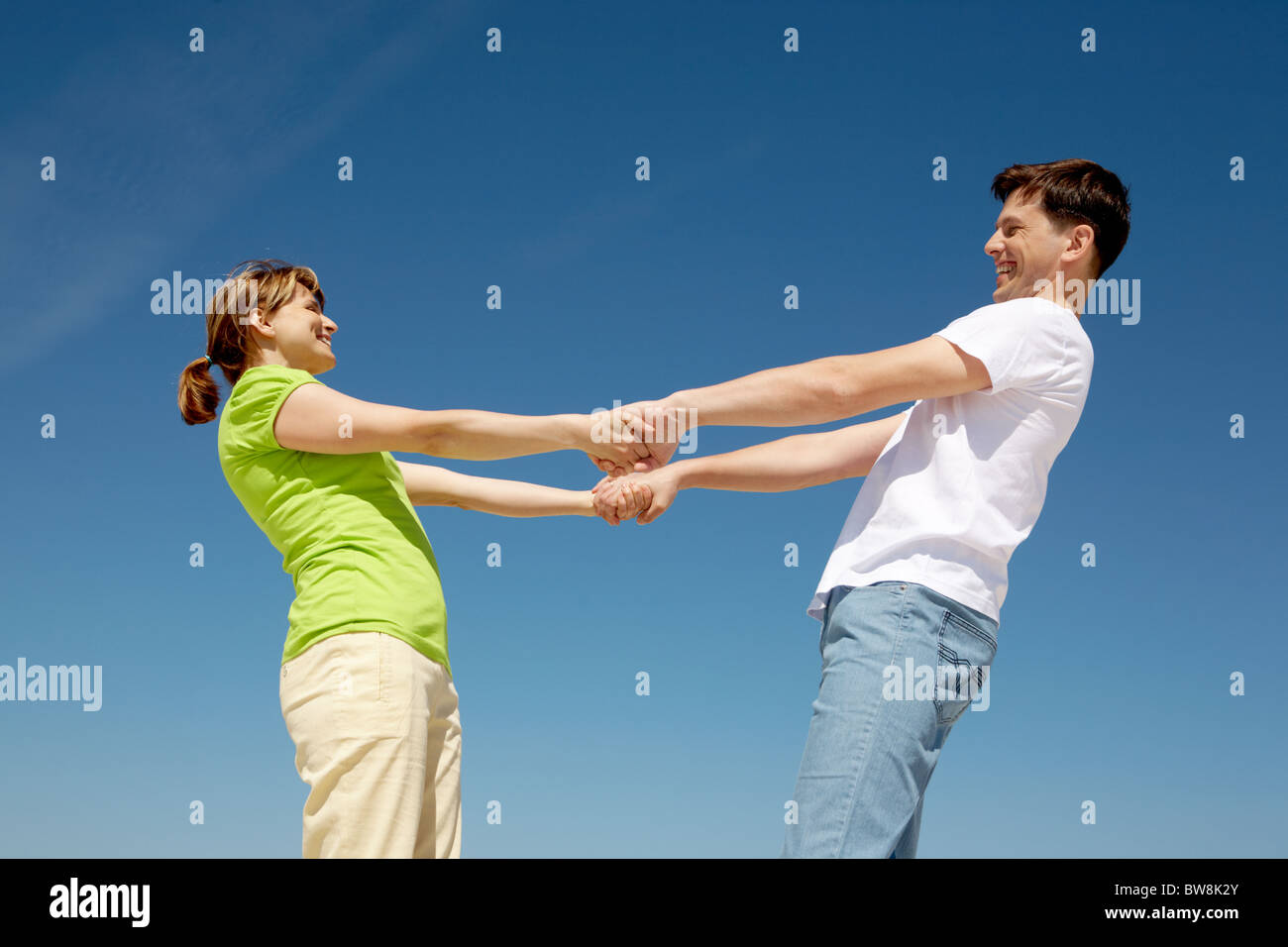 Photo of playful couple holding each other by hands with their arms ...